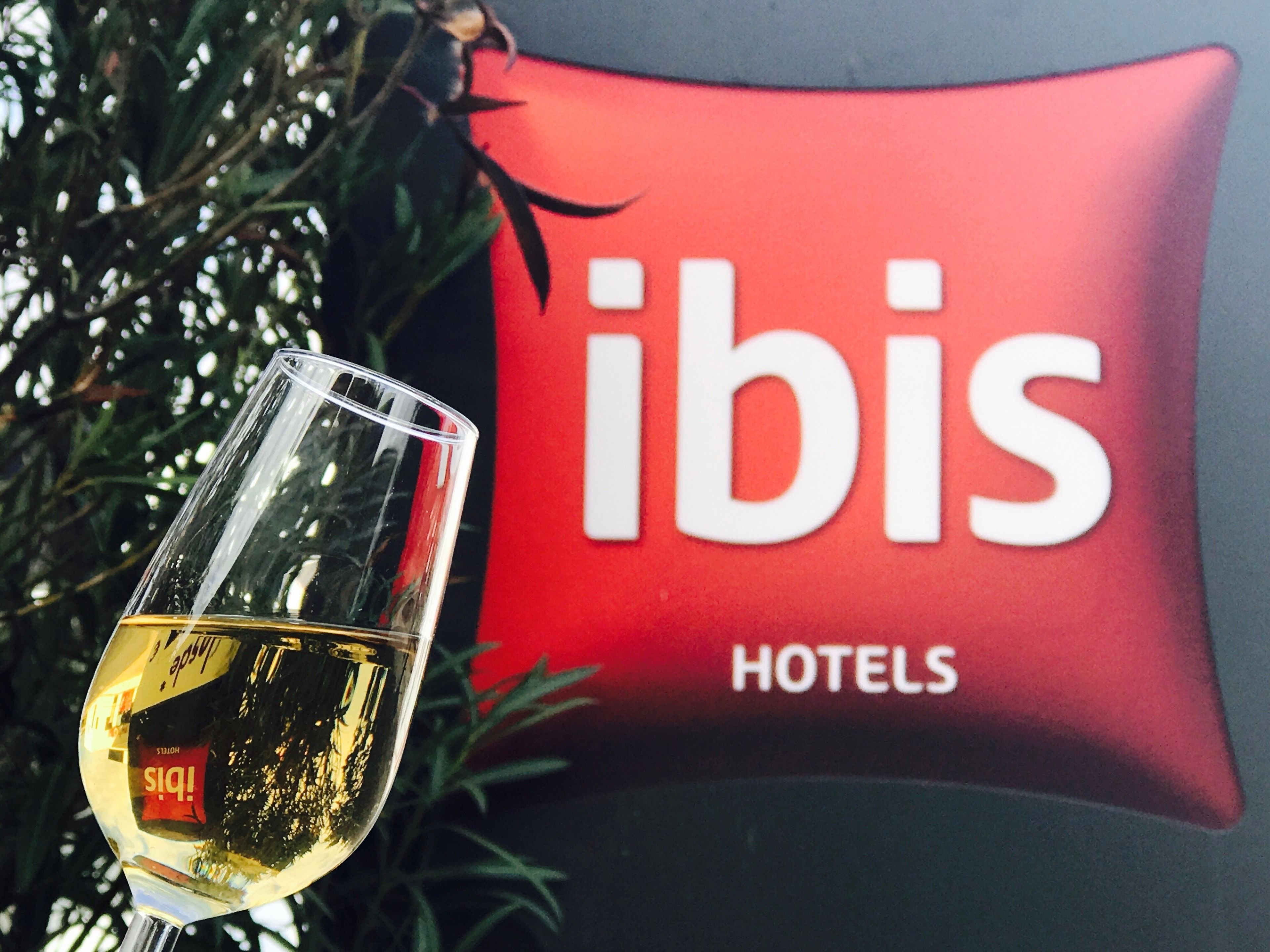 Um copo de vinho ao lado de um travesseiro vermelho com a inscrição 'ibis HOTELS'.
