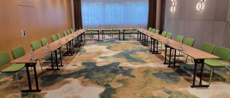 Uma sala de conferências com uma mesa comprida, cadeiras verdes e um tapete estampado.