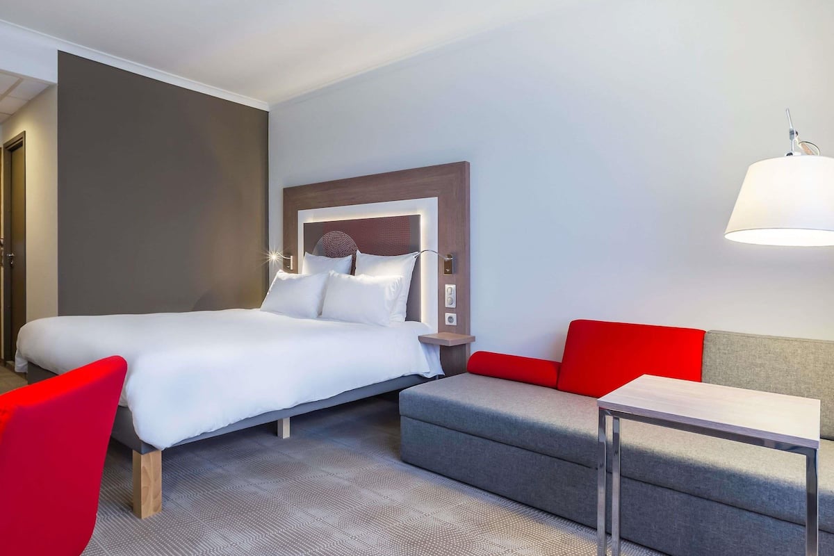 Quarto de hotel com uma cama, uma escrivaninha, uma cadeira e um sofá.