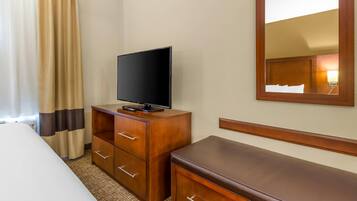 Quarto de hotel com cama, cómoda de madeira, televisão de ecrã plano, espelho e janela com cortinas.
