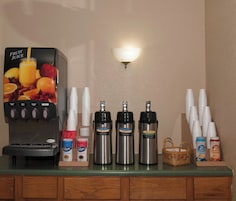 Estação de bebidas com dispensador de suco de fruta, máquinas de café e dispensadores de leite.