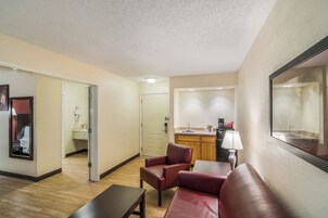 Quarto de hotel com sofá, mesa, cozinha compacta e banheiro visível por uma porta aberta.
