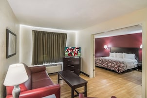 Quarto de hotel com televisão, sofá, escrivaninha, cama e banheiro visível por uma porta aberta.