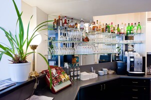 Uma área de bar com prateleiras cheias de garrafas de bebidas, copos e uma máquina de café.