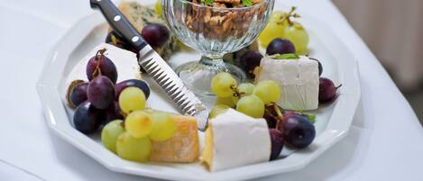 Um prato com queijos variados e uvas, uma faca e uma tigela de vidro com nozes e ervas.