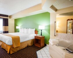 Quarto de hotel com cama, abajures, mesa de cabeceira, banheiro com banheira e espelho.