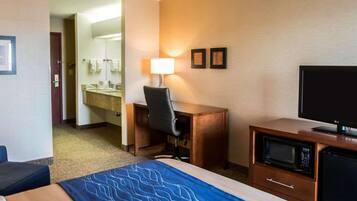 Quarto de hotel com cama, escrivaninha e cadeira, televisão, micro-ondas e banheiro visível por uma porta aberta.