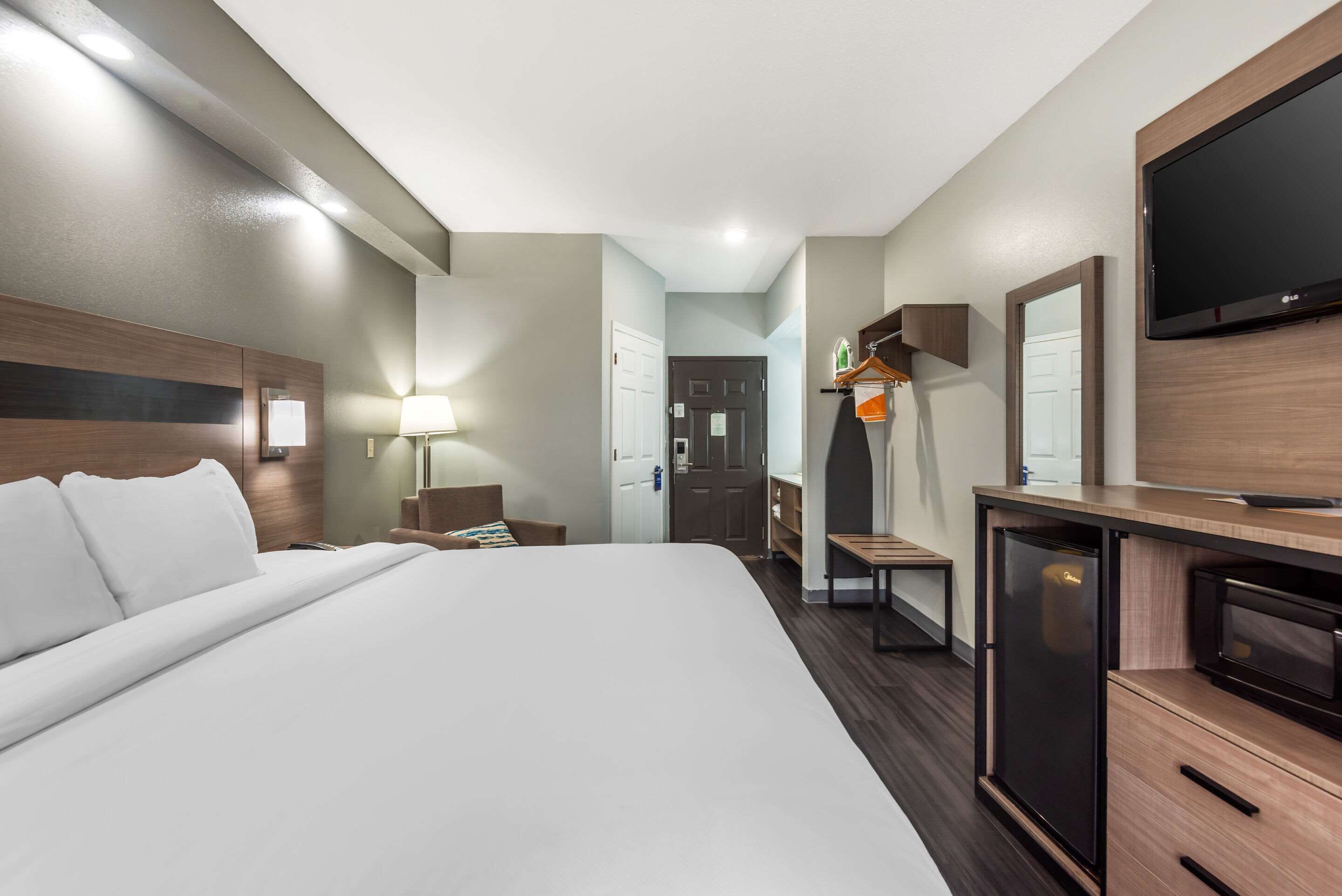 Quarto de hotel com uma cama grande, uma escrivaninha com televisão de tela plana, um guarda-roupa e uma luminária.