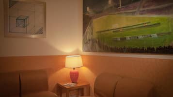 Quarto com pintura de um estádio, luminária em uma mesinha lateral e duas cadeiras.