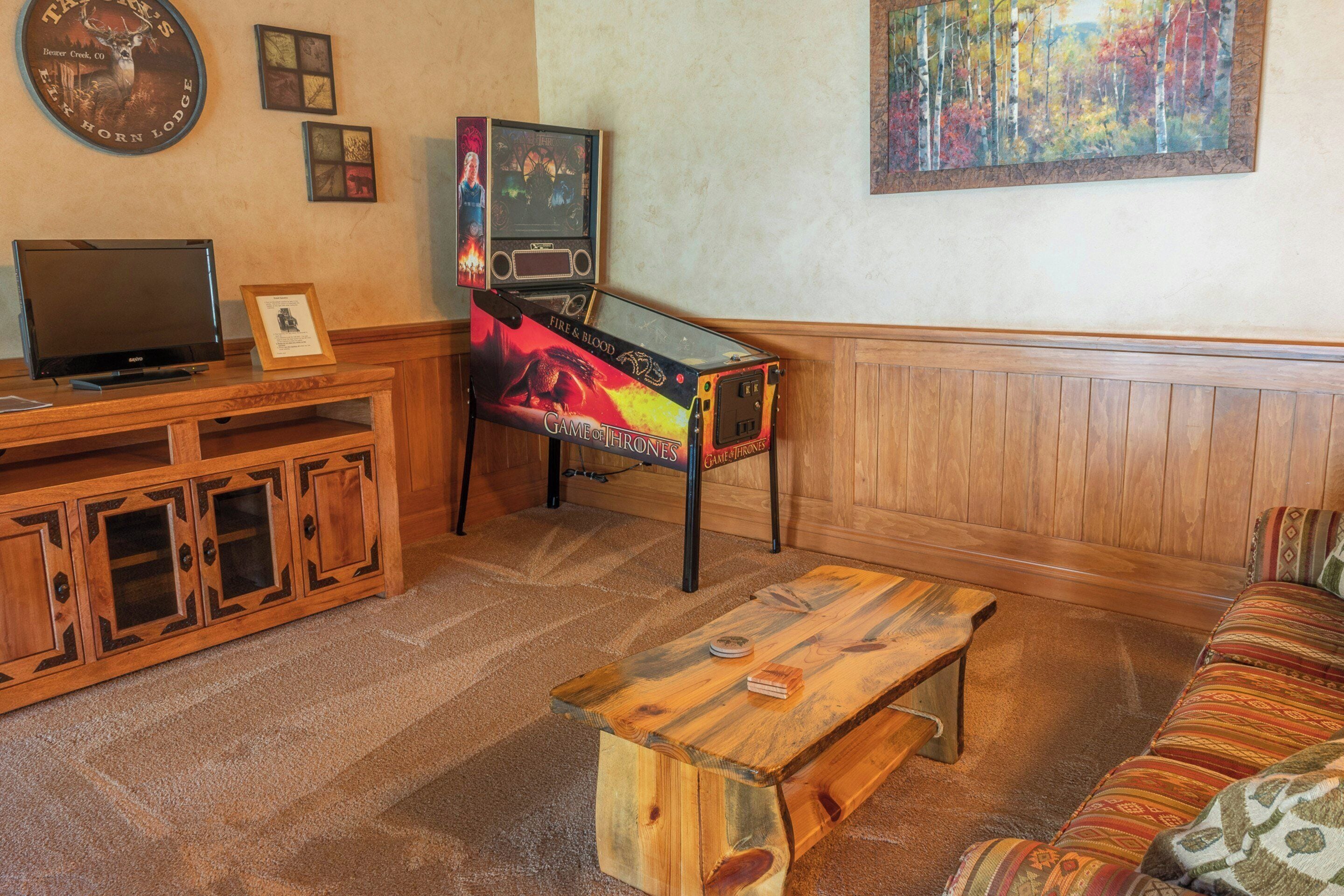 Uma sala de estar acolhedora com um centro de entretenimento de madeira, uma poltrona com tema de Game of Thrones, uma TV de tela plana e um quadro na parede.