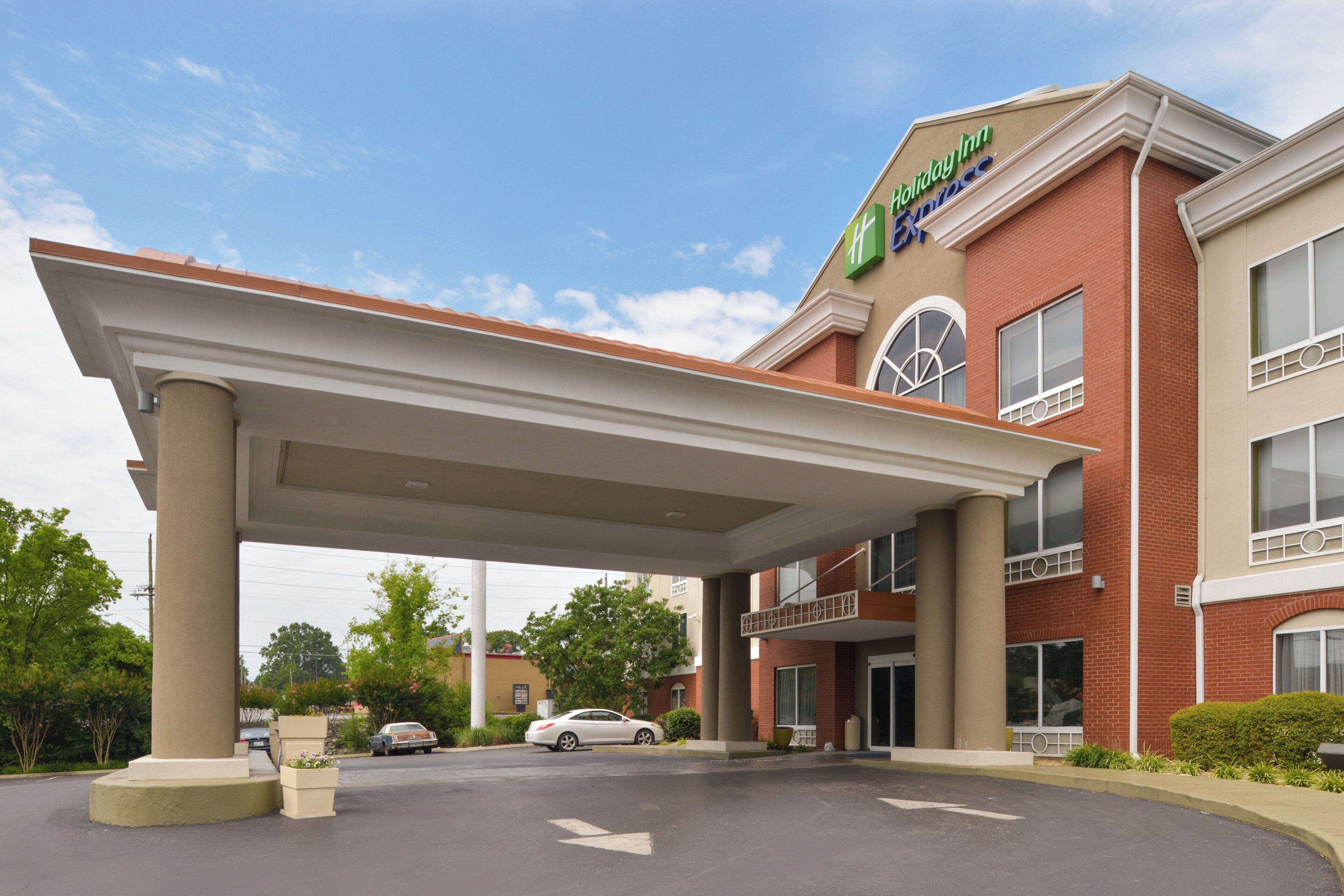 Um hotel Holiday Inn Express com área de estacionamento coberta, fachada de tijolos e céu claro.