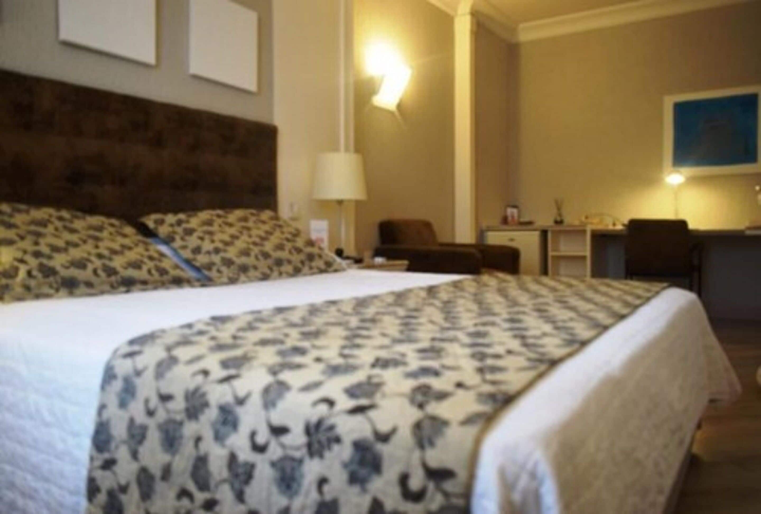 Quarto de hotel com uma cama grande, uma escrivaninha e uma cadeira.