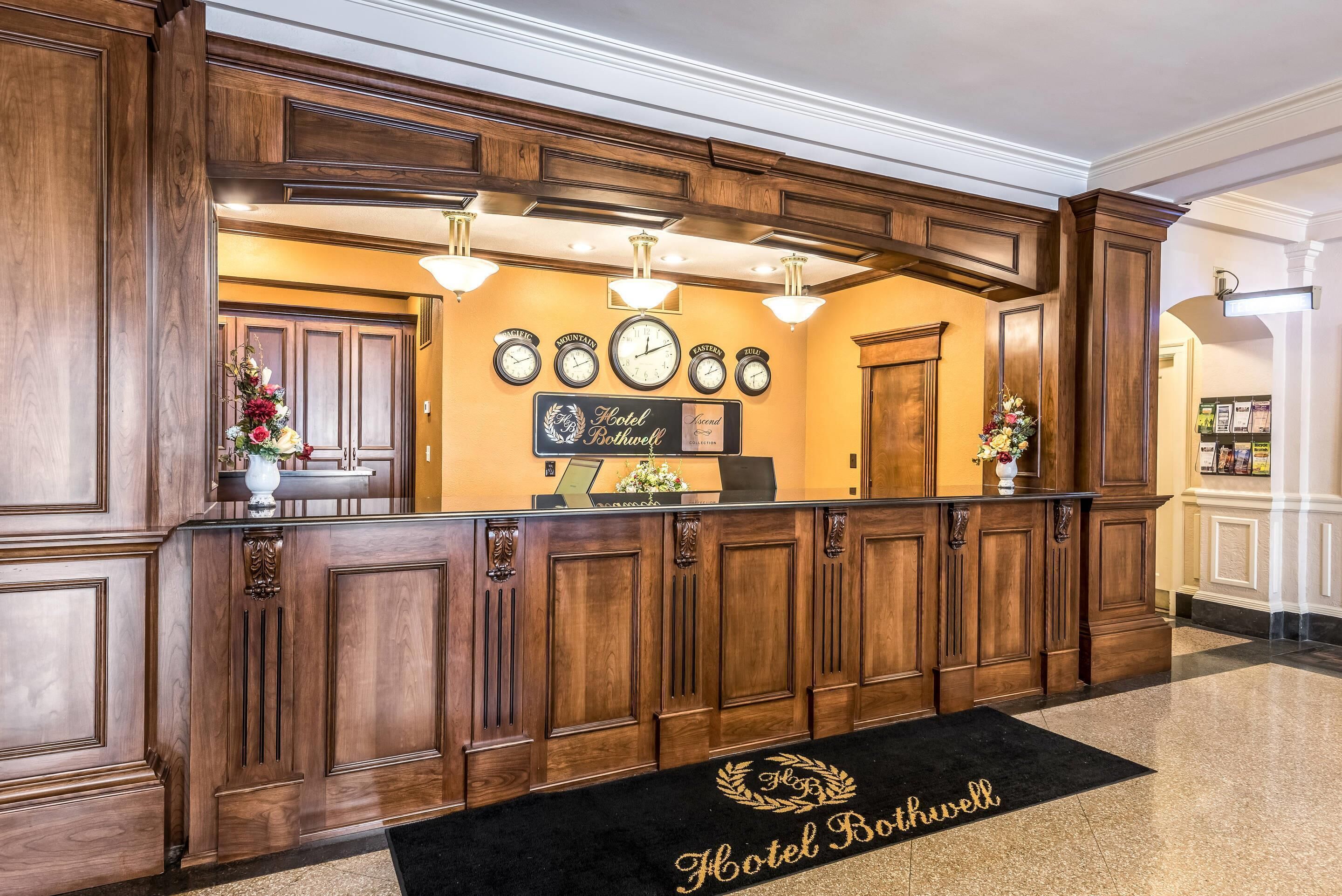 Um balcão de recepção com acabamento em madeira, vários relógios e uma placa com a inscrição 'Hotel Bothwell'.