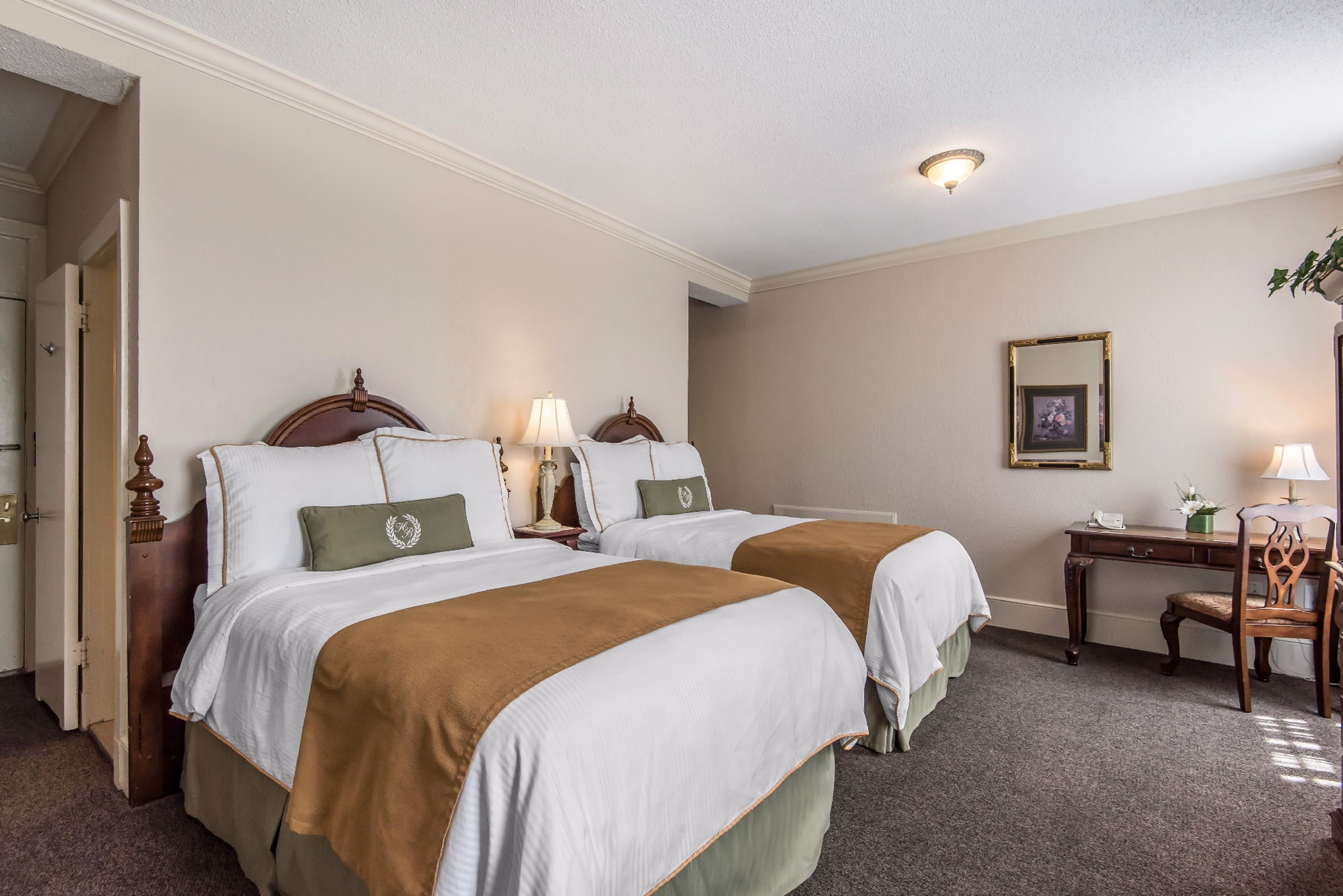 Quarto de hotel com duas camas, uma escrivaninha, uma cadeira e um quadro na parede.