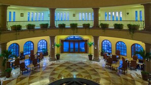 Um hall amplo com piso de azulejos geométricos, vários espaços de estar e grandes janelas.