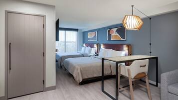 Quarto de hotel com duas camas, uma escrivaninha e uma cadeira.