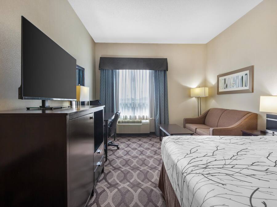 Quarto de hotel com cama, escrivaninha, televisão, sofá e janela com cortinas.