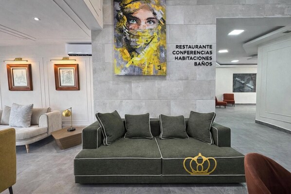 Uma área de estar moderna com sofá, obras de arte emolduradas e uma parede com informações sobre comodidades como restaurante, salas de conferência, acomodações e piscina.