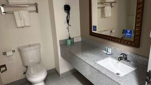 Um banheiro moderno com vaso sanitário branco, pia com bancada de granito, um espelho grande e um porta-toalhas.