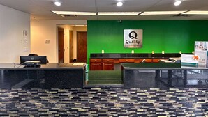 Uma área de recepção de hotel com uma parede verde, um letreiro com a inscrição 'Quality by Choice Hotels' e um balcão de atendimento com um computador.