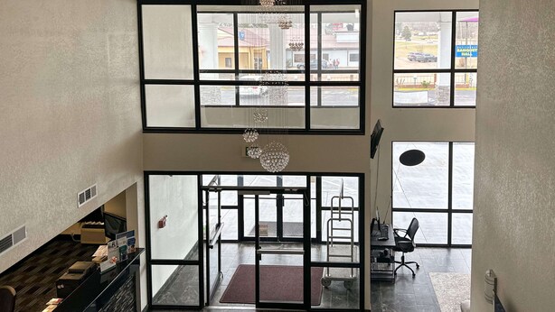 Um saguão de hotel com balcão de recepção, escadaria e vista para o exterior.
