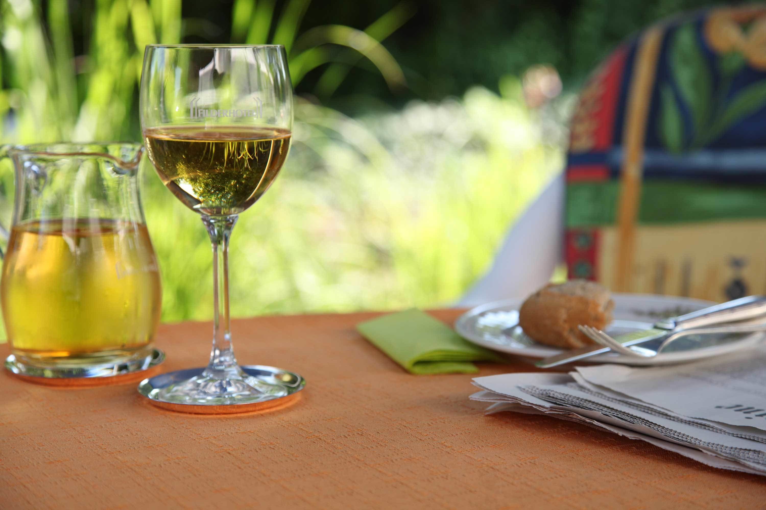 Uma mesa com um copo de vinho branco, um jarro, um prato com um pastel e um garfo.