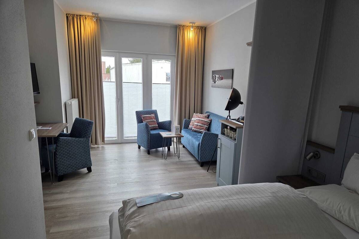 Quarto de hotel com cama, escrivaninha, poltrona, sofá e vista pela janela.