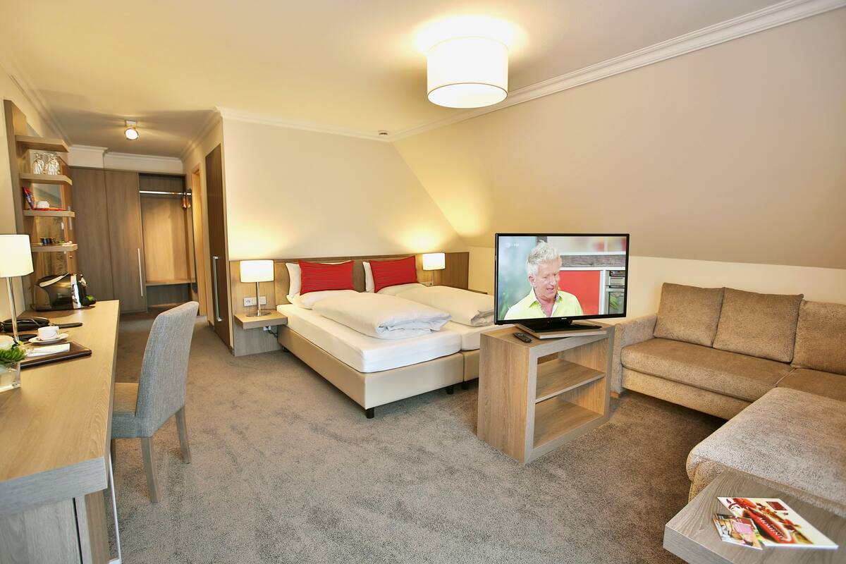 Quarto de hotel com cama, televisão, sofá, escrivaninha e cadeira.