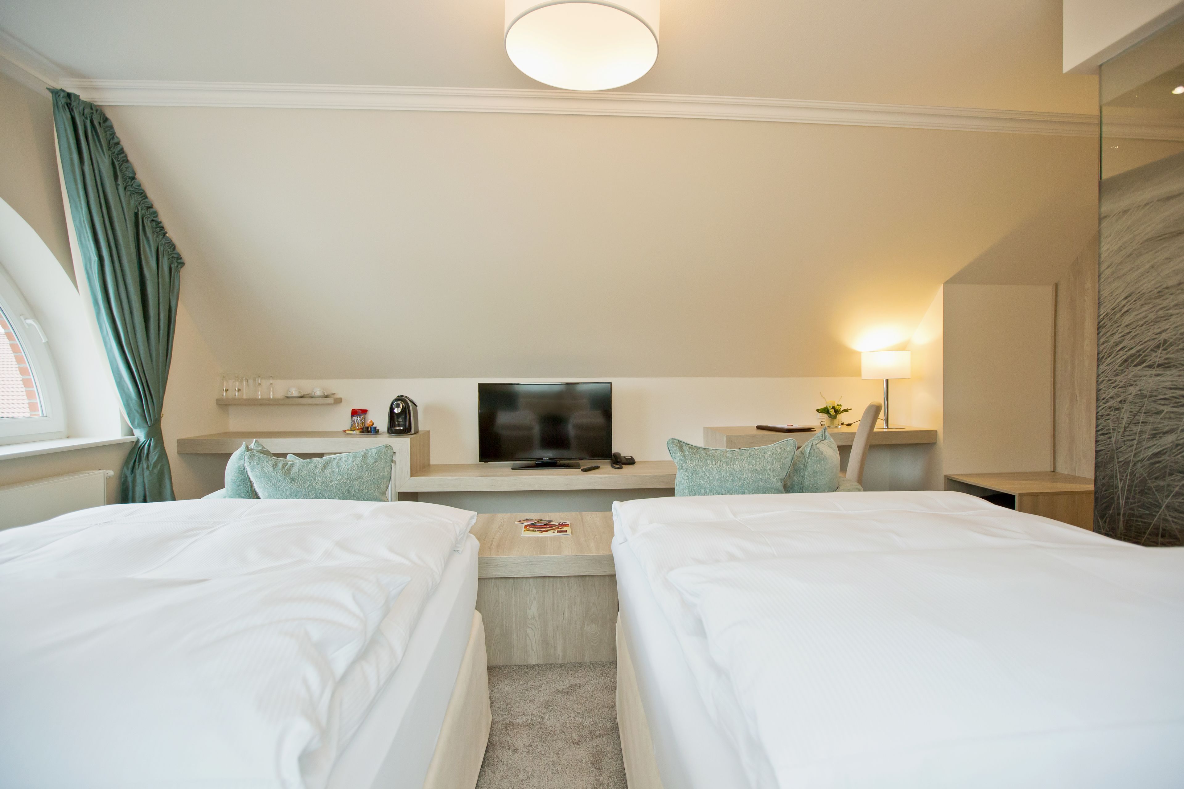 Quarto de hotel com duas camas, televisão, escrivaninha e luminária.