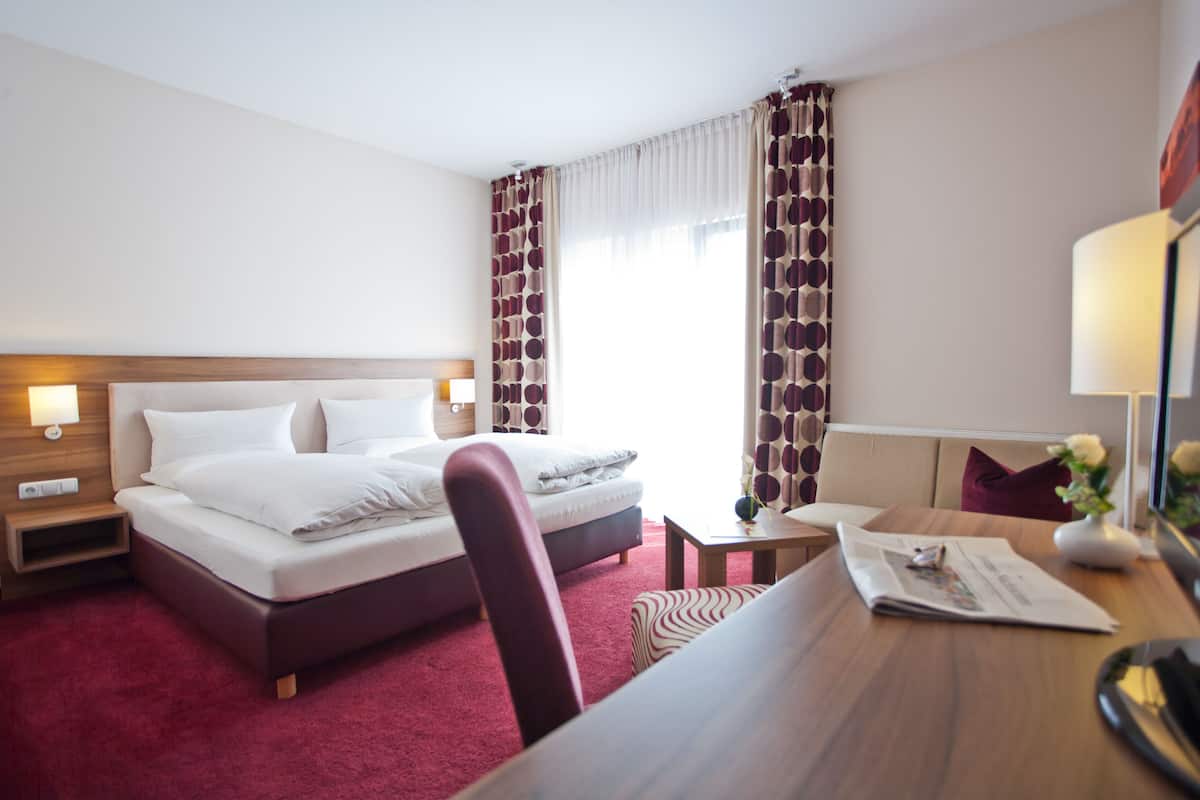 Quarto de hotel com cama, mesas de cabeceira, escrivaninha e uma cadeira.