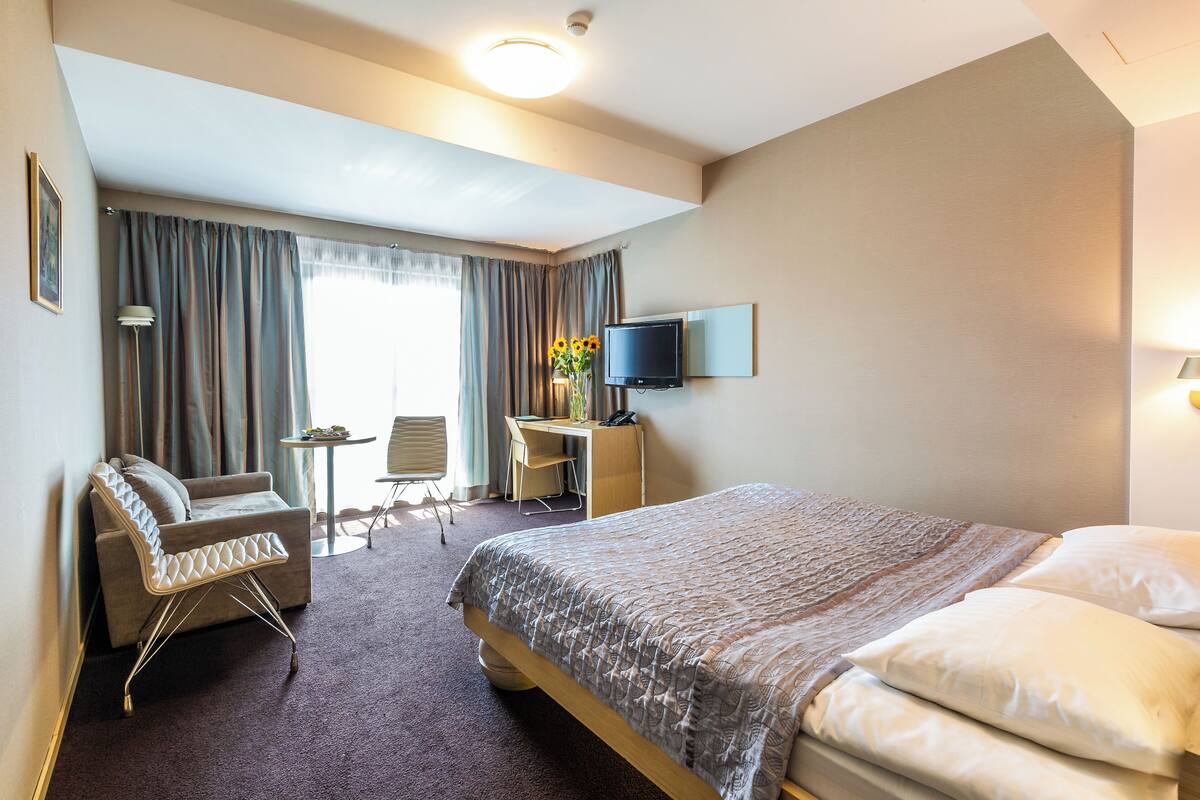 Quarto de hotel com cama, escrivaninha, cadeira e televisão.
