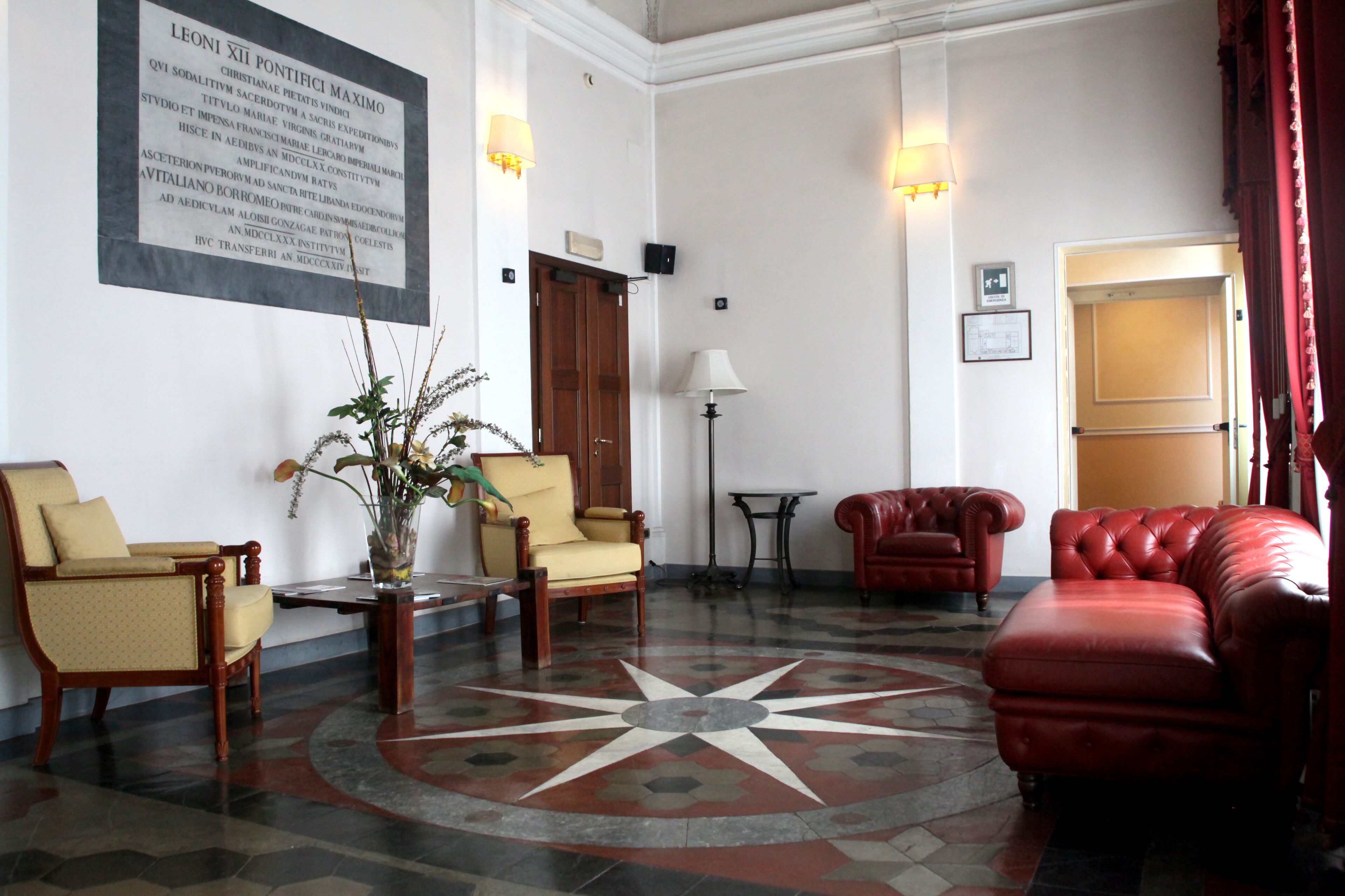 Um hall de entrada com uma placa grande, duas poltronas, um sofá vermelho, um abajur e uma mesa.