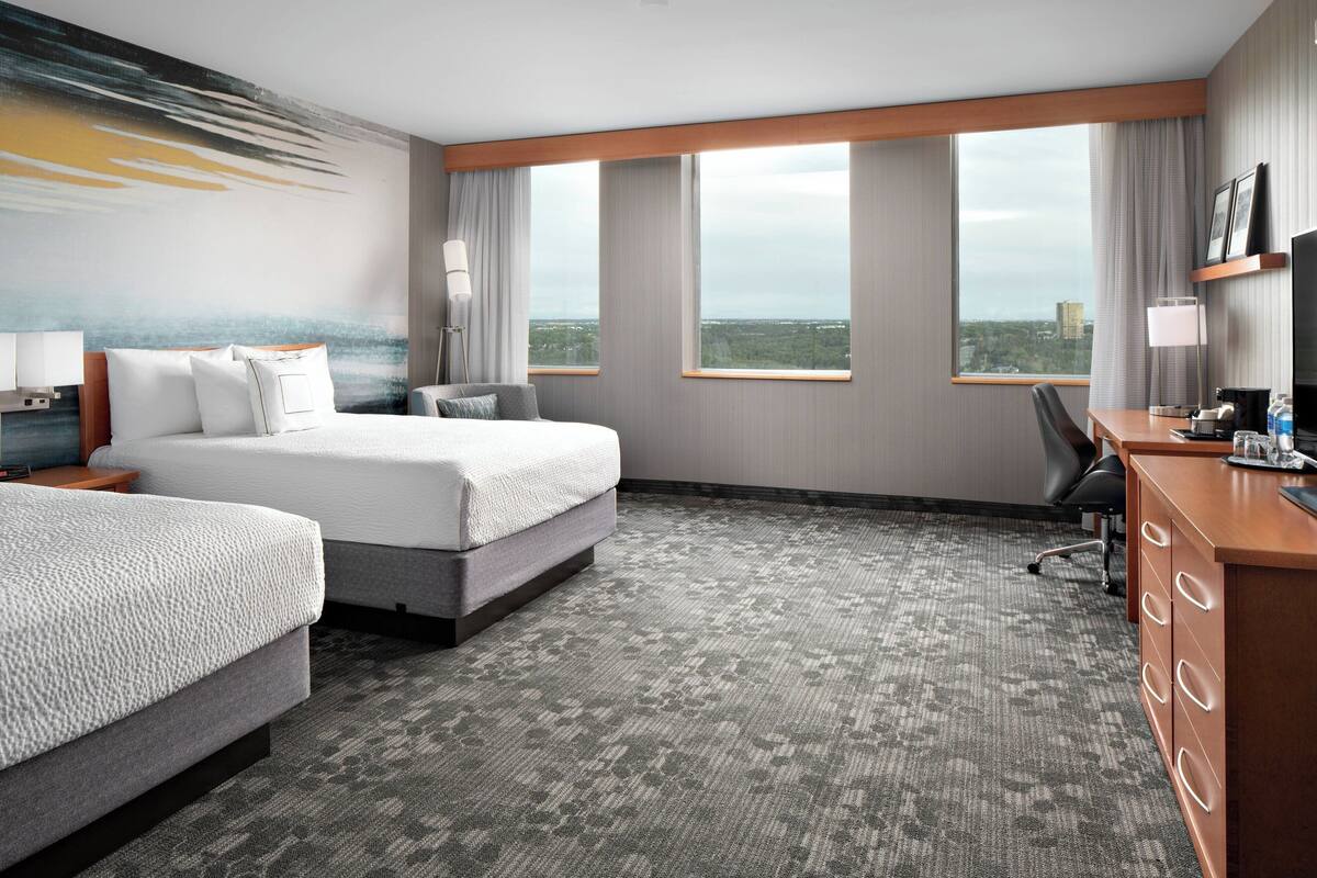 Quarto de hotel com cama grande, escrivaninha, cadeira e vista para a cidade.