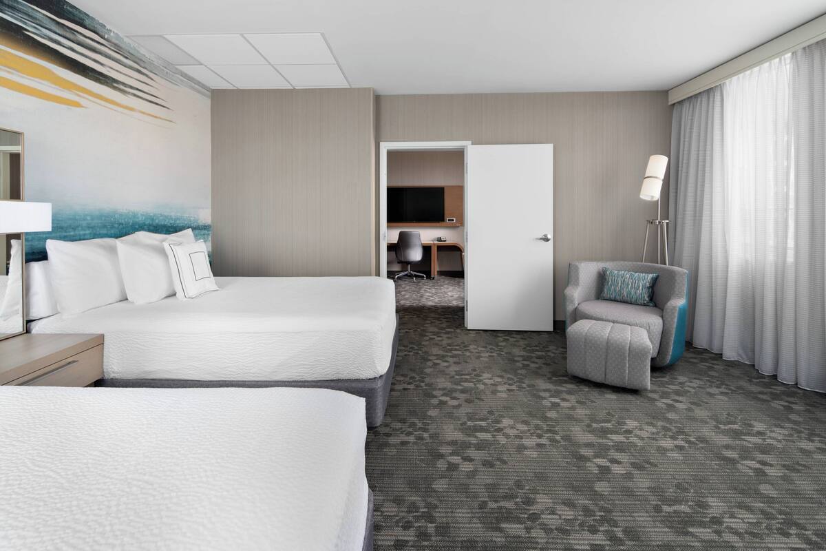 Quarto de hotel com duas camas, uma escrivaninha, uma cadeira e uma televisão.