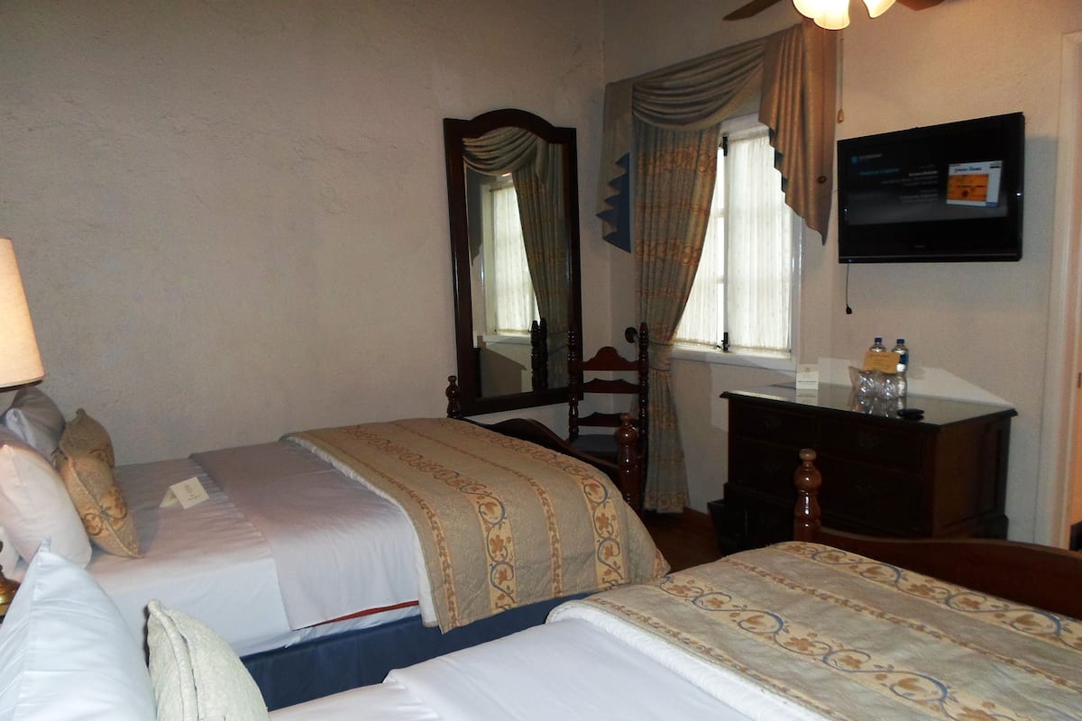 Quarto de hotel com duas camas, um espelho, penteadeira e televisão na parede.