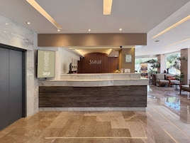 Uma área de recepção de hotel com design moderno, apresentando um balcão de atendimento, espaço de estar e uma grande janela com vista para o exterior.