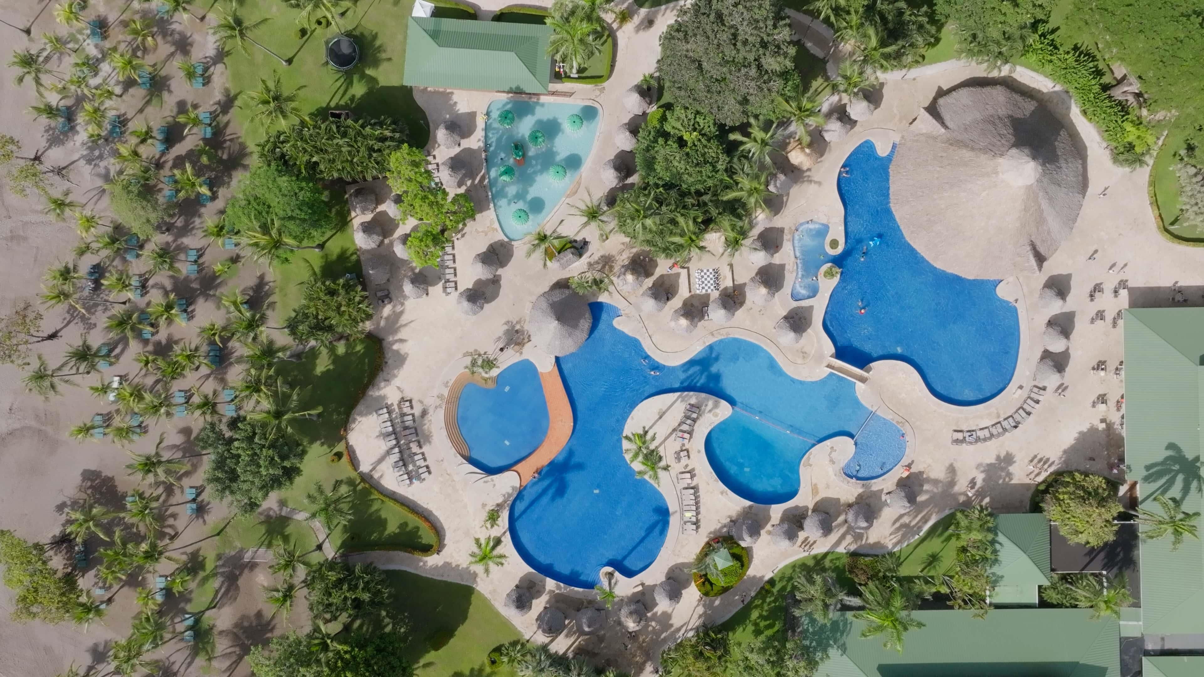Vista aérea de um resort com várias piscinas, palmeiras e áreas de descanso.