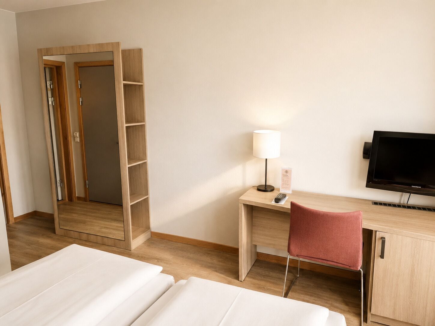 Quarto de hotel com escrivaninha, cadeira, televisão e guarda-roupa.