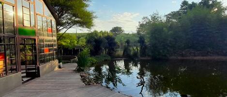 Um deck de madeira junto a um rio calmo, com um edifício com grandes janelas e uma porta de vidro.