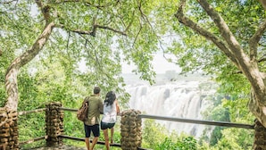 Um casal em uma ponte de pedra admirando uma cachoeira.