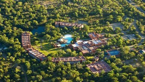 Vista aérea de um resort com vários edifícios, piscina e vegetação ao redor.