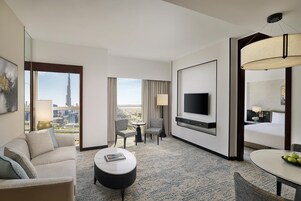 Quarto de hotel com uma janela grande, televisão de tela plana, mesa de jantar e um sofá.