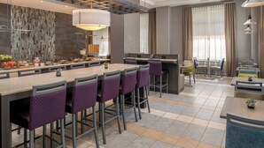 Uma área de refeições moderna com uma mesa comunitária grande, banquetas e um sistema de buffet.