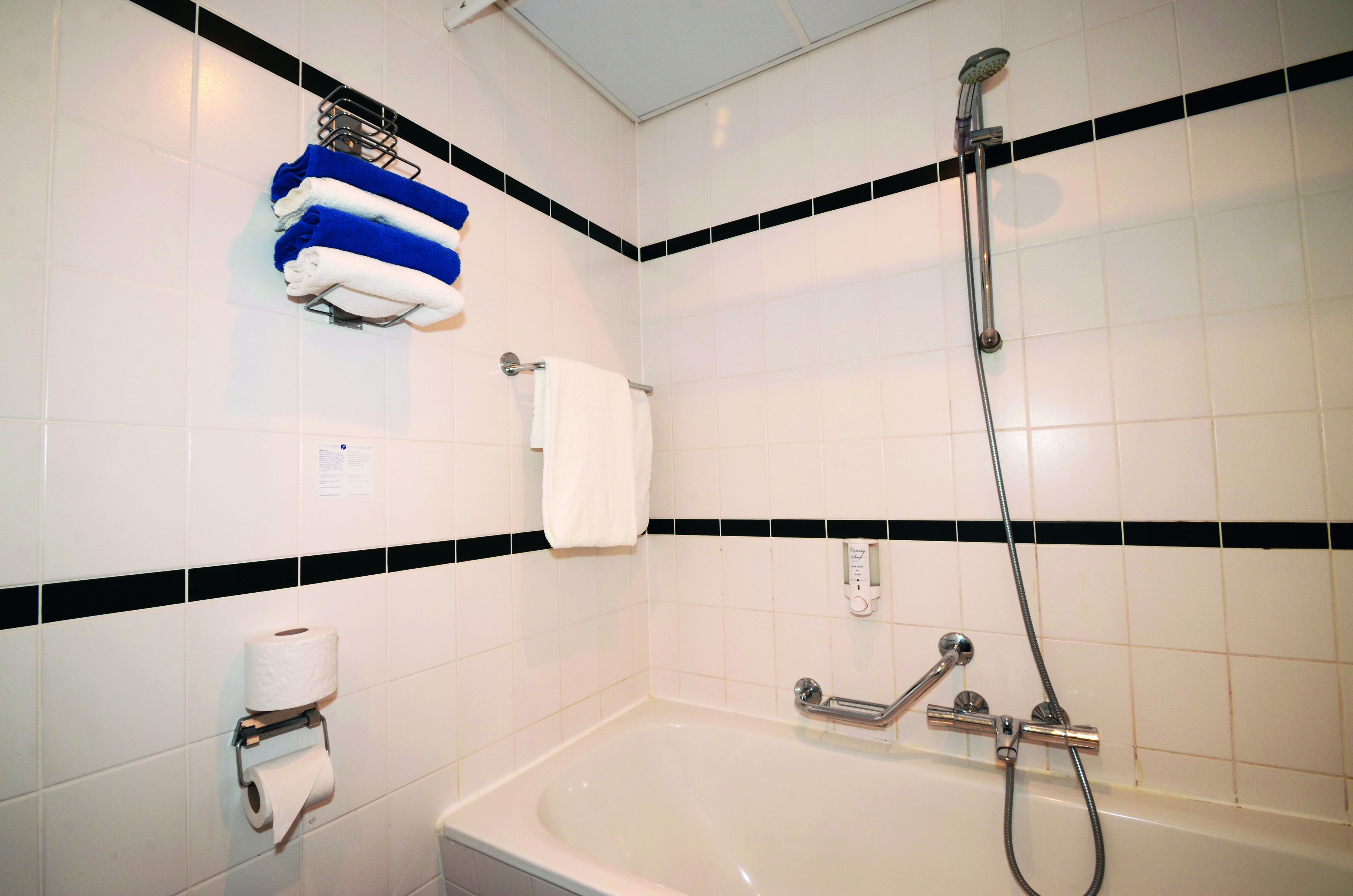 Casa de banho com banheira, chuveiro e porta-toalhas com toalhas dobradas.