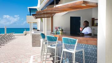 Uma área de bar com vista para o oceano, banquetas e um balcão.