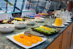Um buffet com diversas frutas, potes de iogurte e um jarro de suco de laranja.