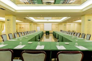 Uma sala de conferências com mesas compridas, cadeiras e uma tela de projeção.