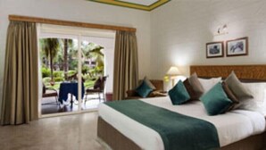 Quarto de hotel com cama, mesa de cabeceira, luminária e vista para um jardim através de uma porta deslizante.