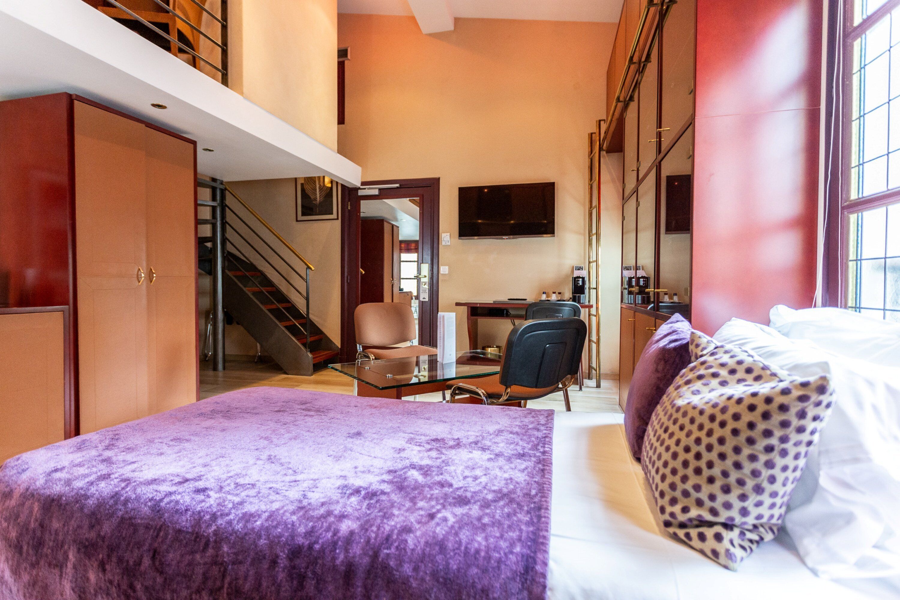 Quarto de hotel espaçoso com uma cama grande, uma escrivaninha e uma escada que leva a um andar superior.