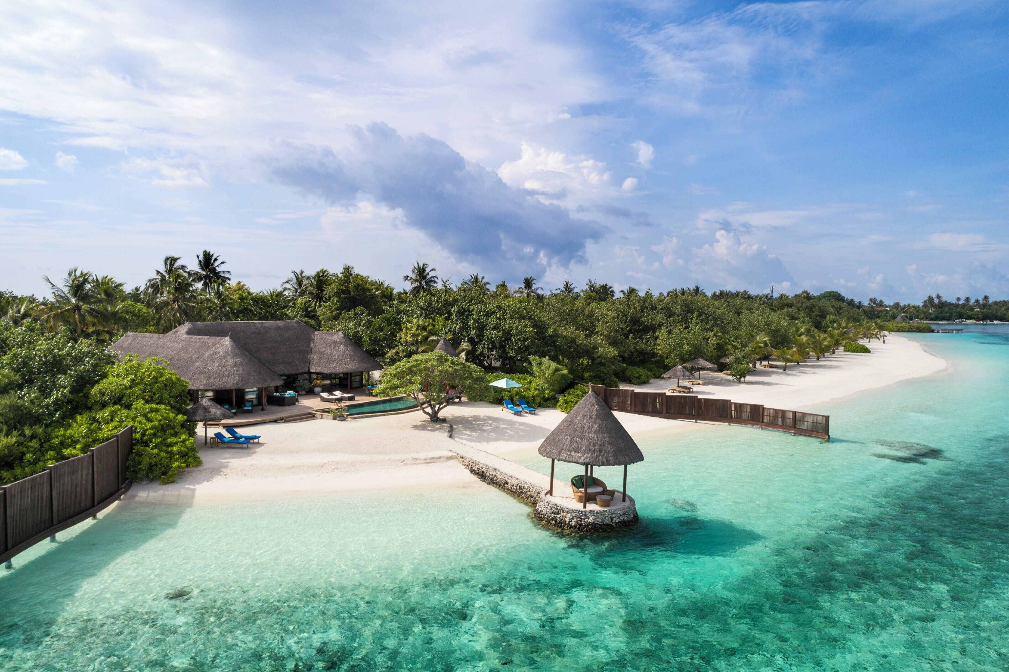 Um resort tropical com bangalôs sobre a água, águas turquesa cristalinas e vegetação exuberante.